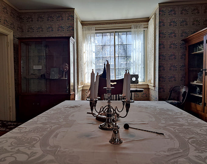 A formal dining setting stays ready for guests, anchored by a classic silver candelabra under soft, natural window light.