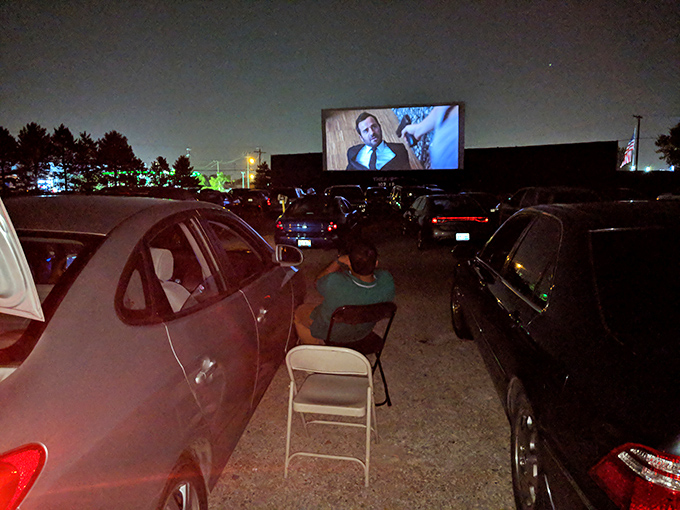 Between cars, a moviegoer settles in with a folding chair for the perfect viewing experience under the stars.