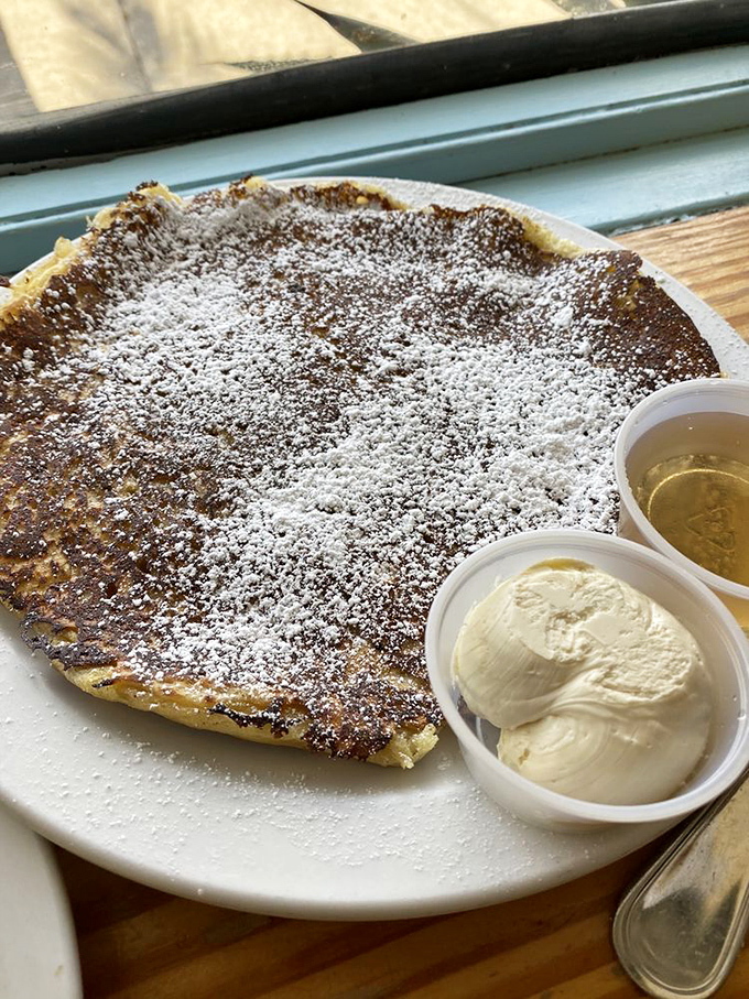 This pancake doesn't just sit on the plate – it commands attention with its golden perfection and generous dusting of powdered sugar.