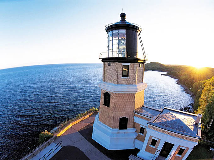 From above, the lighthouse commands a spectacular panorama of Lake Superior's vastness. The morning light bathes the structure in a golden glow against the blue expanse.