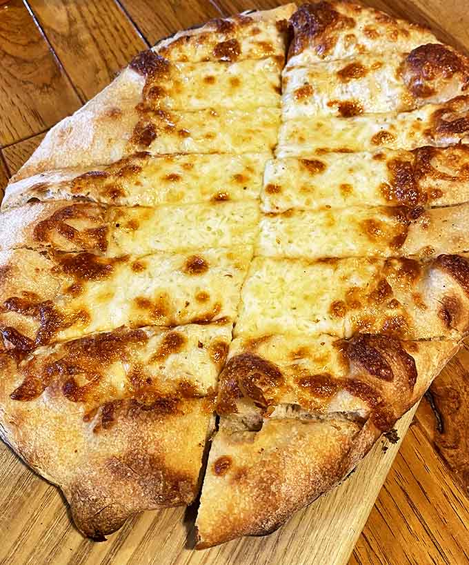 The cheesebread glistens with golden perfection, promising a stretchy, gooey interior that makes sharing nearly impossible.