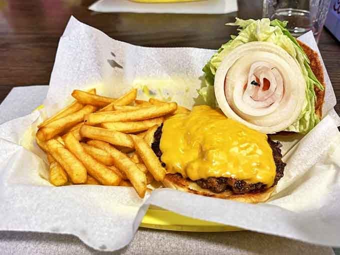 A hand-formed patty crowned with melted American cheese on a pillowy bun, accompanied by a generous portion of perfectly crisp fries.