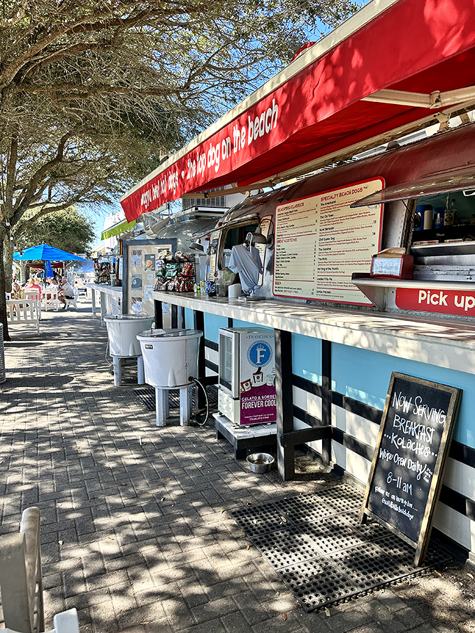 The hot dog stand's bright red awning creates a cheerful contrast against the silver trailer, drawing hungry beachgoers like a culinary lighthouse.