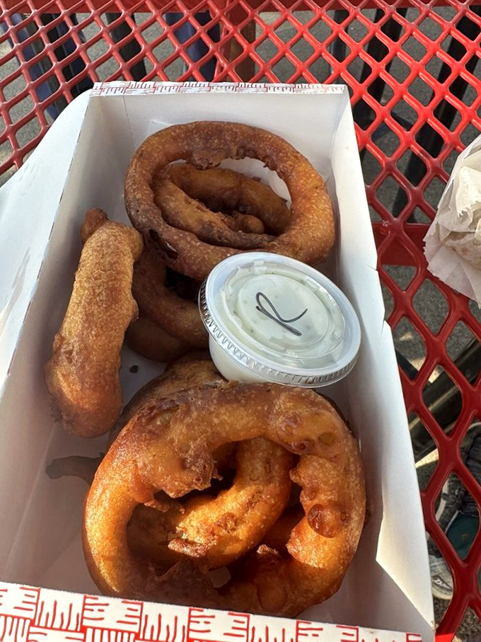 Golden onion rings stacked high in their paper container &ndash; each one a crispy, savory halo of deep-fried perfection. 