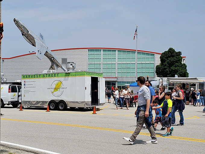 A sunny day brings aviation enthusiasts outdoors, where food trucks and displayed aircraft create a festival atmosphere during special events.