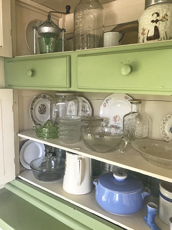 Mint-green cabinets frame Depression glass and everyday dishes – beautiful utilitarian objects from when households cherished what they owned.