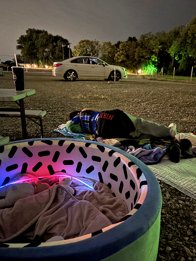 As night falls, the glow of the screen illuminates faces of all ages, united in the simple joy of movies under stars.