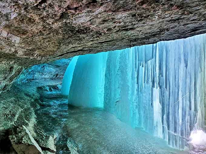 Behind the frozen falls, an ethereal blue ice cave forms – nature's secret room that rewards those brave enough to venture inside.