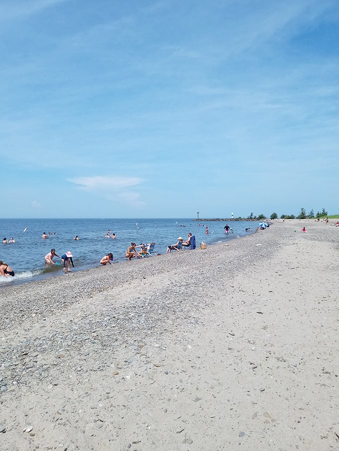 Beach-goers dot the shoreline like colorful confetti, each finding their perfect spot along this uncrowded stretch of Lake Erie paradise.