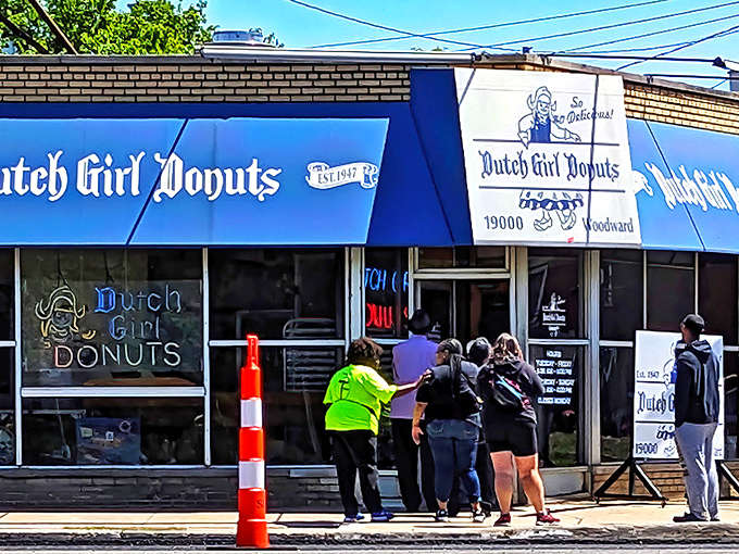 The iconic blue awning of Dutch Girl Donuts stands as a beacon for sweet-toothed pilgrims on Woodward Avenue, promising 24-hour donut bliss.