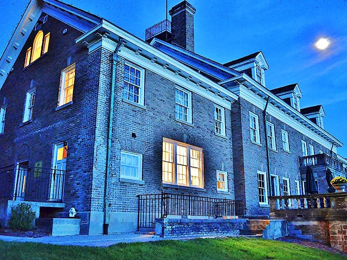 Exterior: Twilight transforms this stately brick mansion into a glowing time capsule, its windows like warm eyes watching over decades of Michigan history.