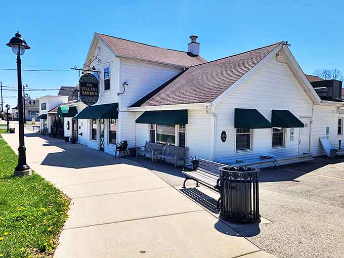The Village Tavern's white clapboard exterior stands proudly in Long Grove, its vintage sign and green awnings welcoming visitors like an old friend.