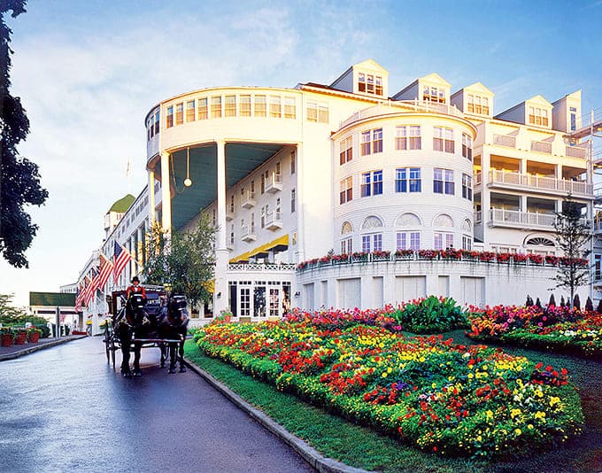 The Grand Hotel stands majestically against Michigan's blue sky, its iconic white fa&ccedil;ade and green-roofed grandeur welcoming visitors like a Victorian dream come true.