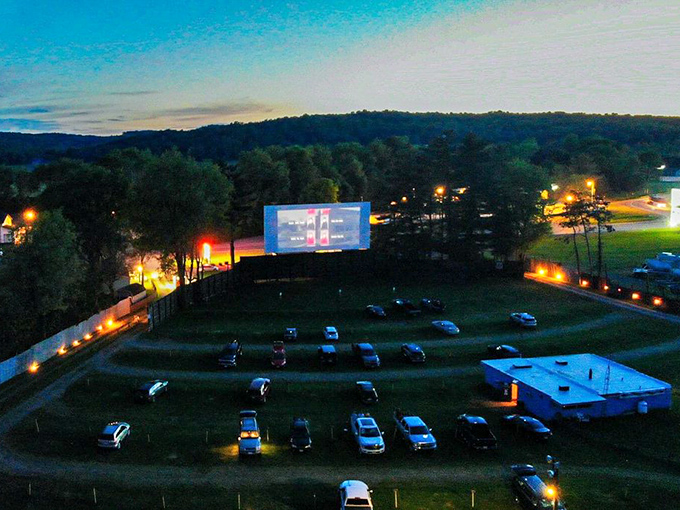Twilight magic descends as cars gather beneath the massive screen, headlights dimming while anticipation brightens at Lynn Drive-In Theatre.