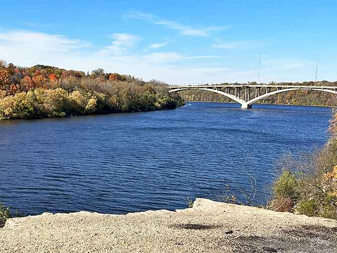 The mighty Mississippi flows beneath the historic Ford Parkway Bridge, framed by autumn foliage that transforms Shadow Falls Park into a painter's dream.