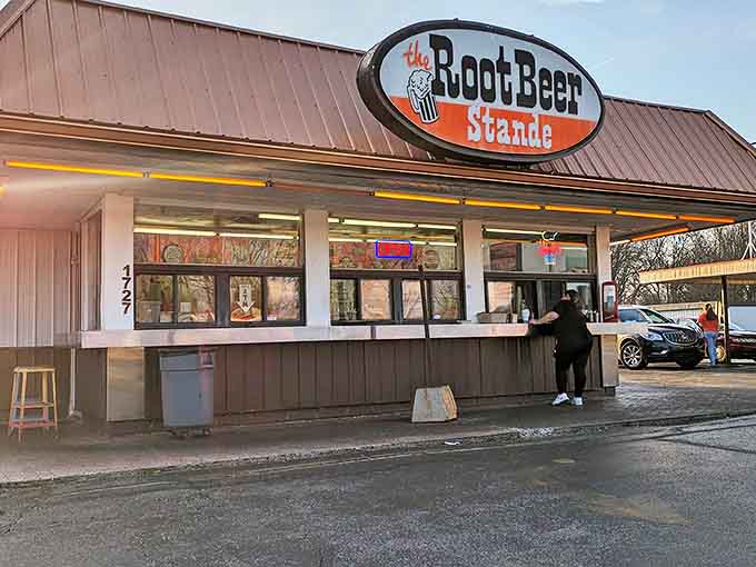 The iconic oval sign of The Root Beer Stande beckons hungry travelers with promises of nostalgic delights and carhop service.