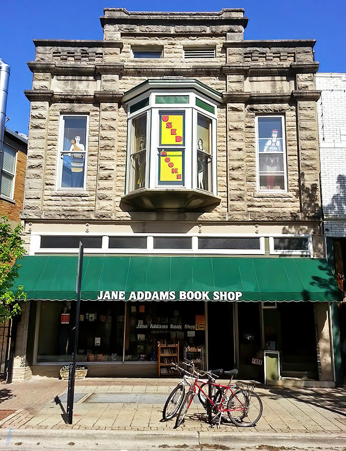 The historic limestone facade of Jane Addams Book Shop stands proudly on Neil Street, its bay window like a lighthouse for literary souls seeking harbor.