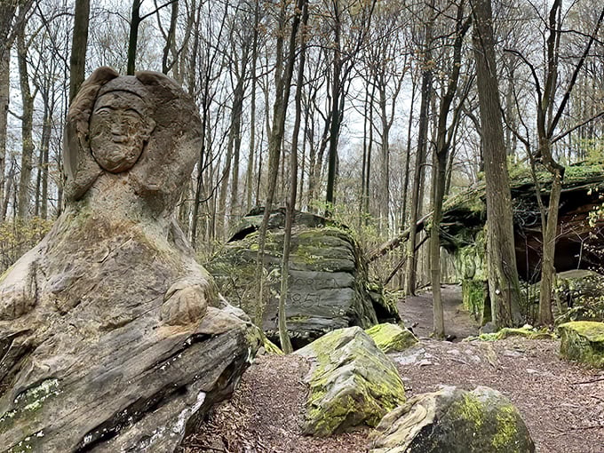 Ancient stone watches silently as visitors pass, its weathered face a testament to Noble Stuart's artistic vision among the trees.