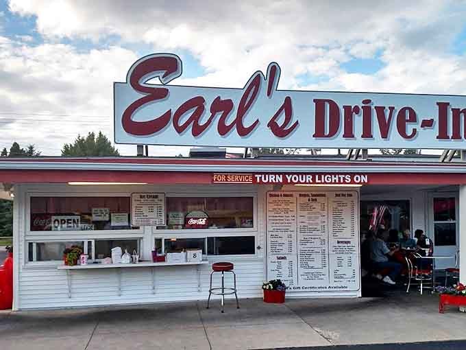 The iconic red script of Earl's Drive-In sign beckons hungry travelers with its timeless promise: "FOR SERVICE TURN YOUR LIGHTS ON." Classic Americana at its finest.