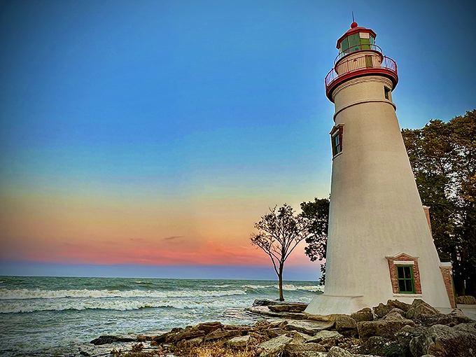 The Marblehead Lighthouse stands majestically against a sunset sky, its white tower glowing with the day's last light – a postcard-perfect moment captured in real life.