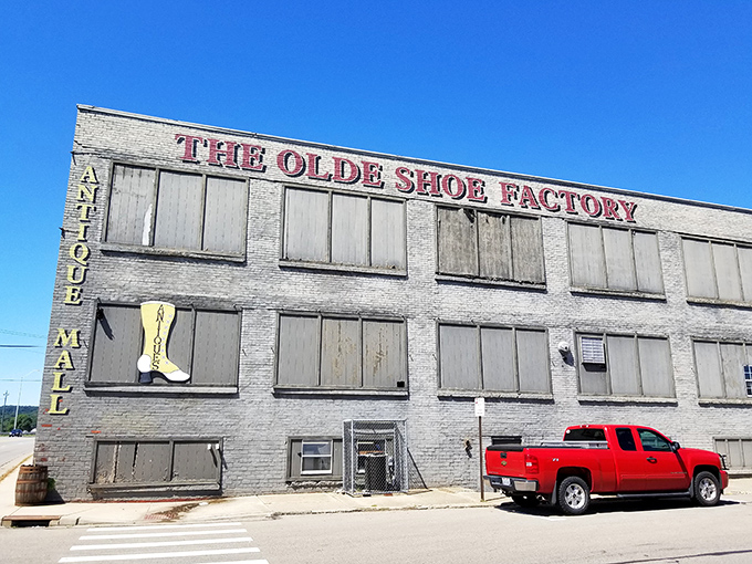 The imposing brick facade of The Olde Shoe Factory stands as a time capsule, its weathered sign promising adventures in antiquing.