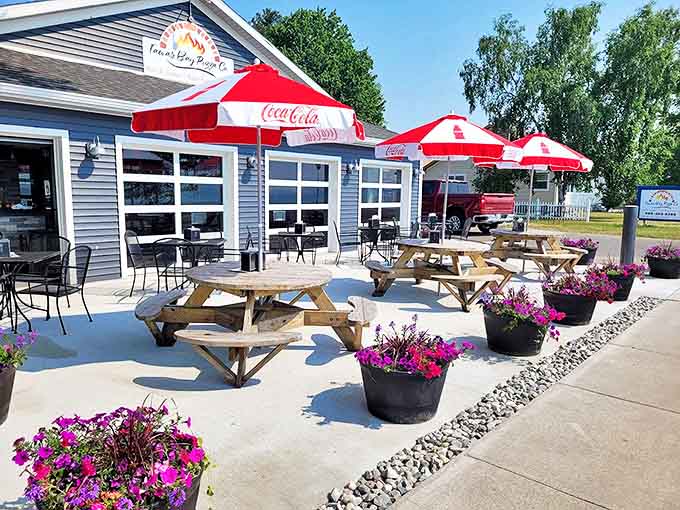 The inviting exterior of Tawas Bay Pizza Co., where red umbrellas and colorful flowers welcome hungry travelers to pizza paradise.
