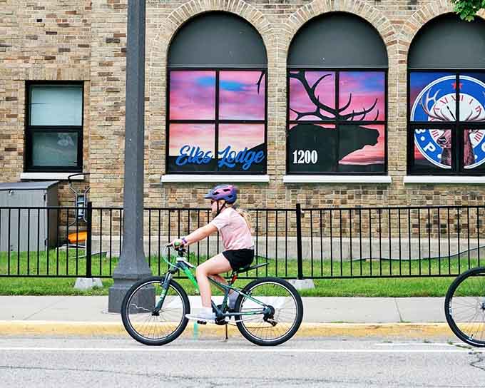 A young cyclist cruises past creative window displays, enjoying the town's bike-friendly streets and artistic spirit.