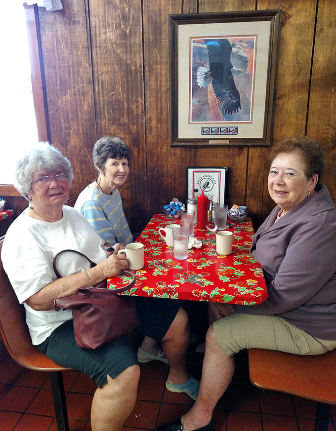 Three generations of wisdom gather around a festive tablecloth, their conversation flowing as freely as the coffee in this timeless social sanctuary.