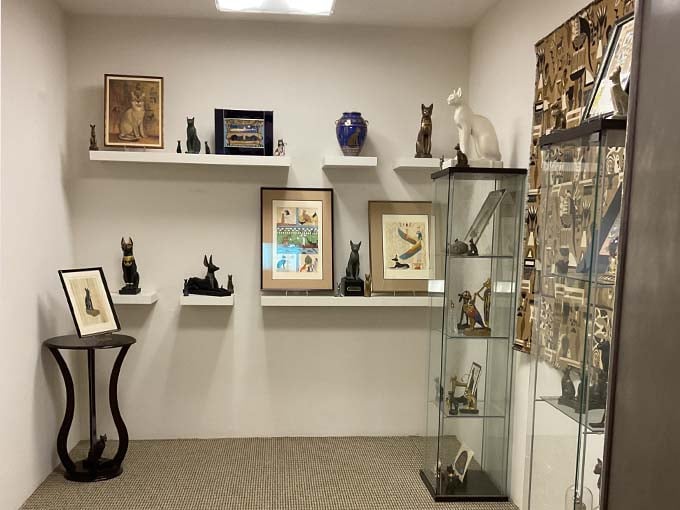 Shelves lined with cat figurines and statues from around the world demonstrate how feline worship transcends cultural boundaries.