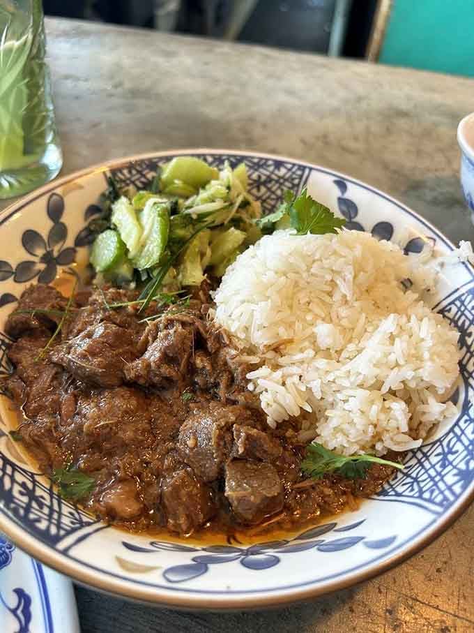 Beef rendang with rice and pickled vegetables, a plate that balances rich, savory meat with bright, tangy accompaniments like a culinary tightrope walker.