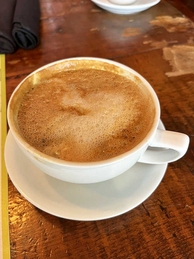 A proper latte with foam so perfect it seems almost a shame to disturb it, served on a rustic wooden table that's seen countless caffeine revelations.