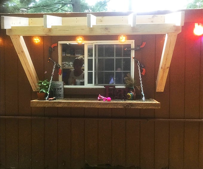 This charming outdoor window shelf glows with cozy lights, perfect for casual backyard drink orders.