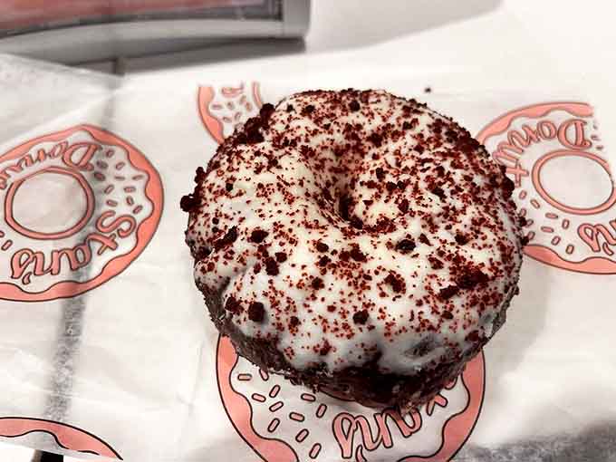 This red velvet donut wears its cream cheese frosting like a crown, with crumbs that look like ruby dust &ndash; royalty in the donut kingdom.