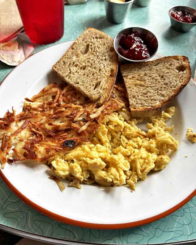 Simple pleasures done right: fluffy scrambled eggs, perfectly crisped hash browns, and hearty toast served with homemade jam that tastes like summer in a jar.
