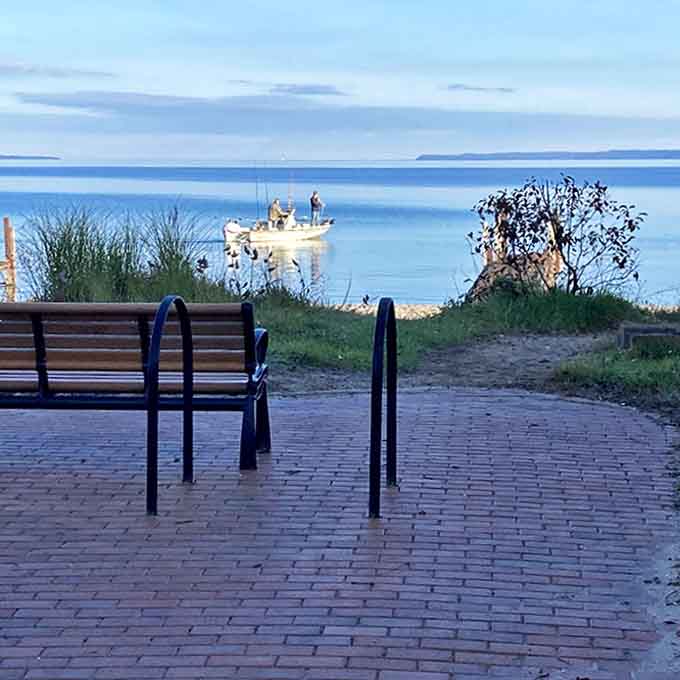 A peaceful bench invites contemplation as fishing boats dot the horizon, proving some screens are worth watching.