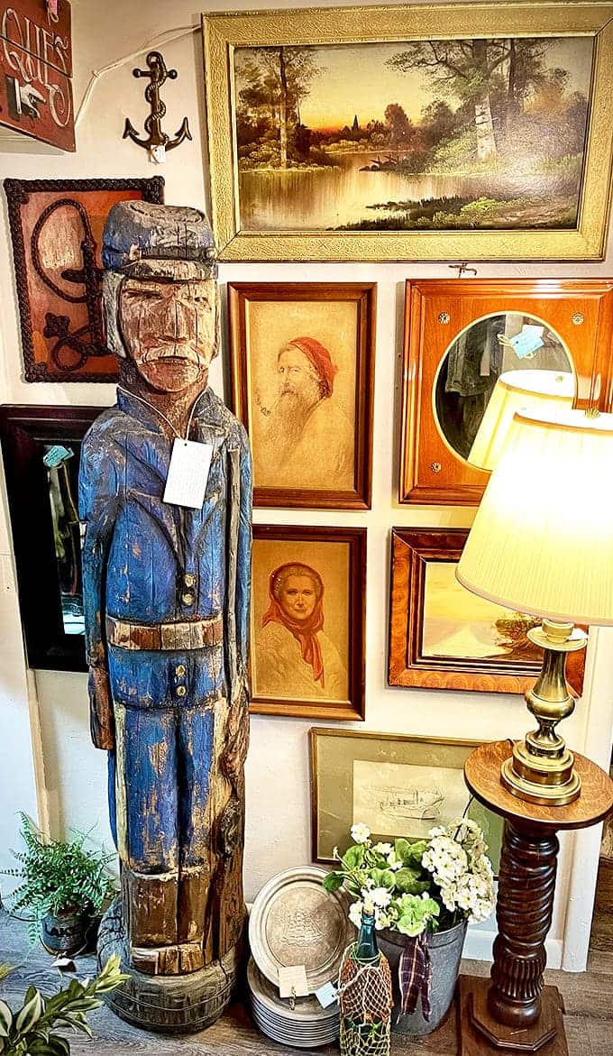 Vintage Art & D&eacute;cor Display Wall: This wooden sailor stands sentinel among a gallery of framed memories, like a guardian of stories from Michigan's maritime past.