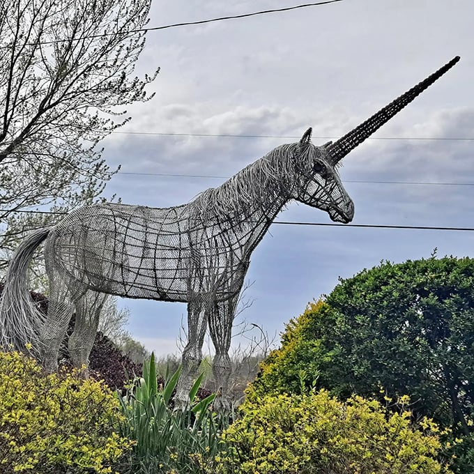 The wire-frame unicorn catches sunlight in its delicate construction, creating an almost ghostly apparition among the flowering bushes.