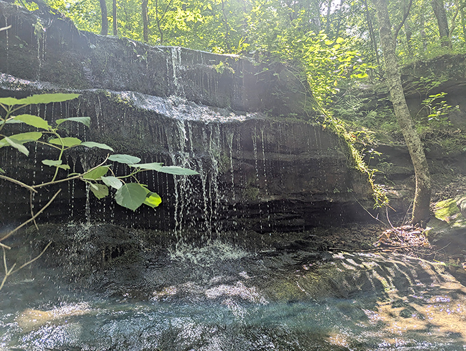 Delicate waterfall curtains the dark stone, creating nature's own spa treatment for weary hikers.