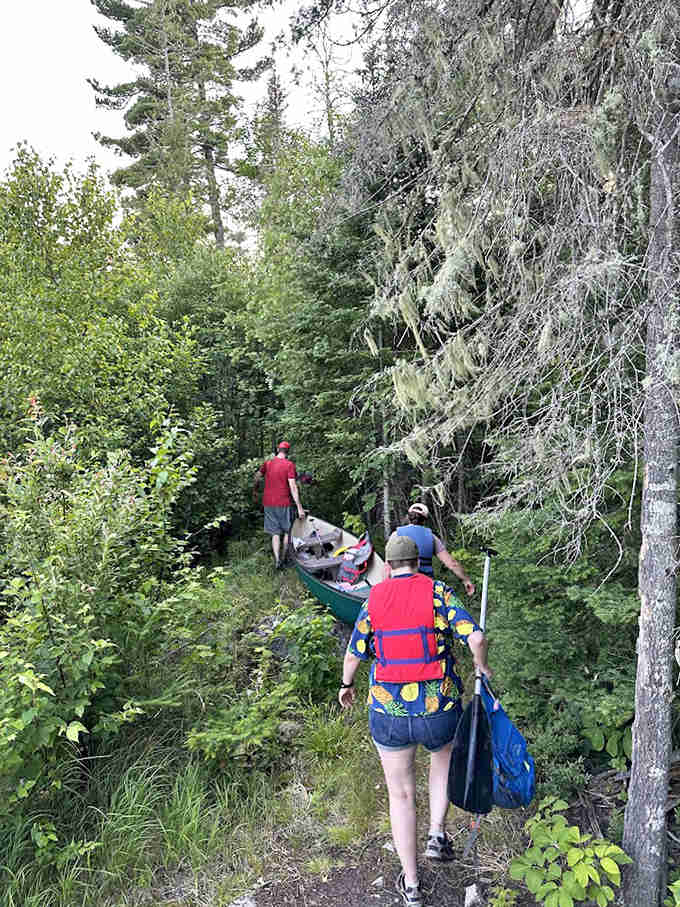 Adventurers portage their canoe through dense woodland, proving some journeys still require more effort than just pressing "navigate."