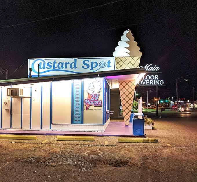 Custard Spot's illuminated sign transforms the night, creating an irresistible glow that draws dessert seekers like moths to a flame. The iconic cone sculpture stands tall against the evening sky.