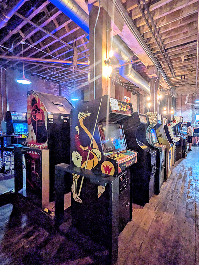 A row of lovingly maintained arcade cabinets lines the exposed brick wall, their screens glowing with invitation and possibility.