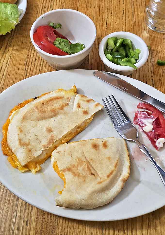Cheese Quesadilla: Golden-brown tortillas reveal a molten cheese interior, accompanied by fresh tomatoes and crisp cucumbers for a simple yet satisfying meal.