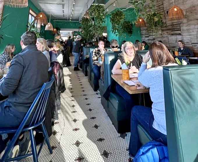 The narrow dining room buzzes with energy as patrons enjoy their Southeast Asian feast, surrounded by lush plants and vibrant decor.