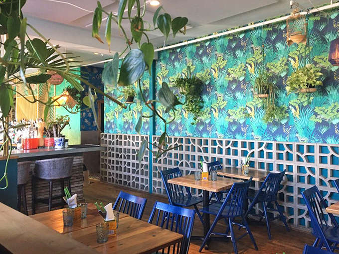 The tropical wallpaper and hanging plants create a space that feels like dining in a stylish friend's vacation home rather than a restaurant.