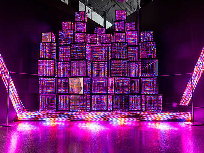 Glowing cubes stack like a futuristic cityscape, pulsing with purple light that transforms the geometric forms into something almost alive.