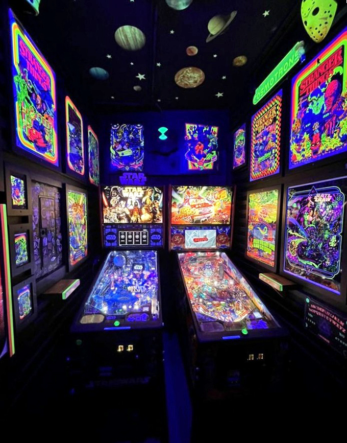 The pinball room glows with blacklight-reactive artwork, creating a psychedelic cave where flippers, bumpers, and silver balls reign supreme.