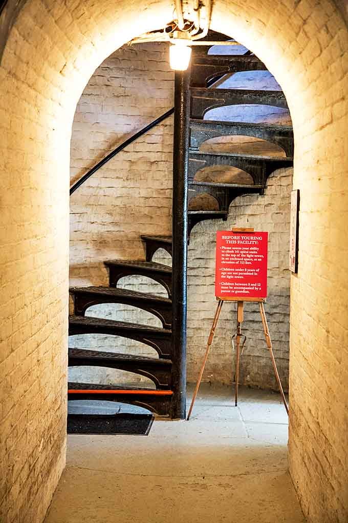 The entrance to the spiral staircase beckons adventurous visitors, its curved brick archway framing the beginning of a 113-foot vertical journey through maritime history.