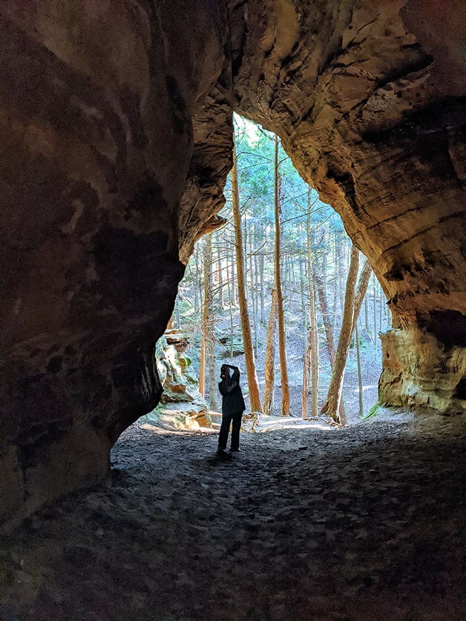 Scale and perspective: A silhouetted visitor stands in awe at the cave's entrance, providing perfect scale to this massive natural formation.