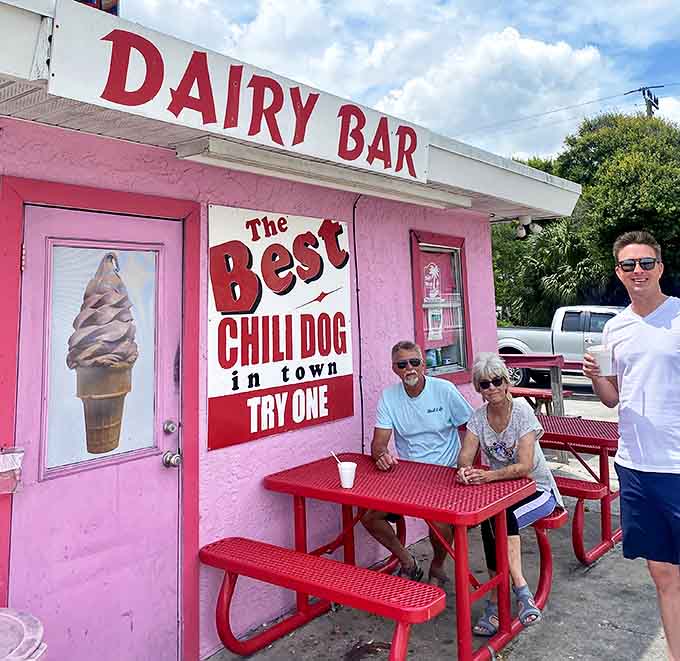 Three generations of happiness gathered around a red picnic table, proving that the best family traditions often involve chili dogs and soft serve.