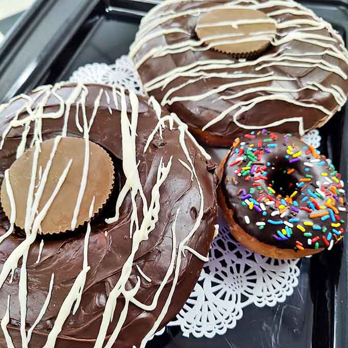 Giant glazed donuts lounging on their trays, waiting to be adopted by someone with a serious sweet tooth and zero willpower.